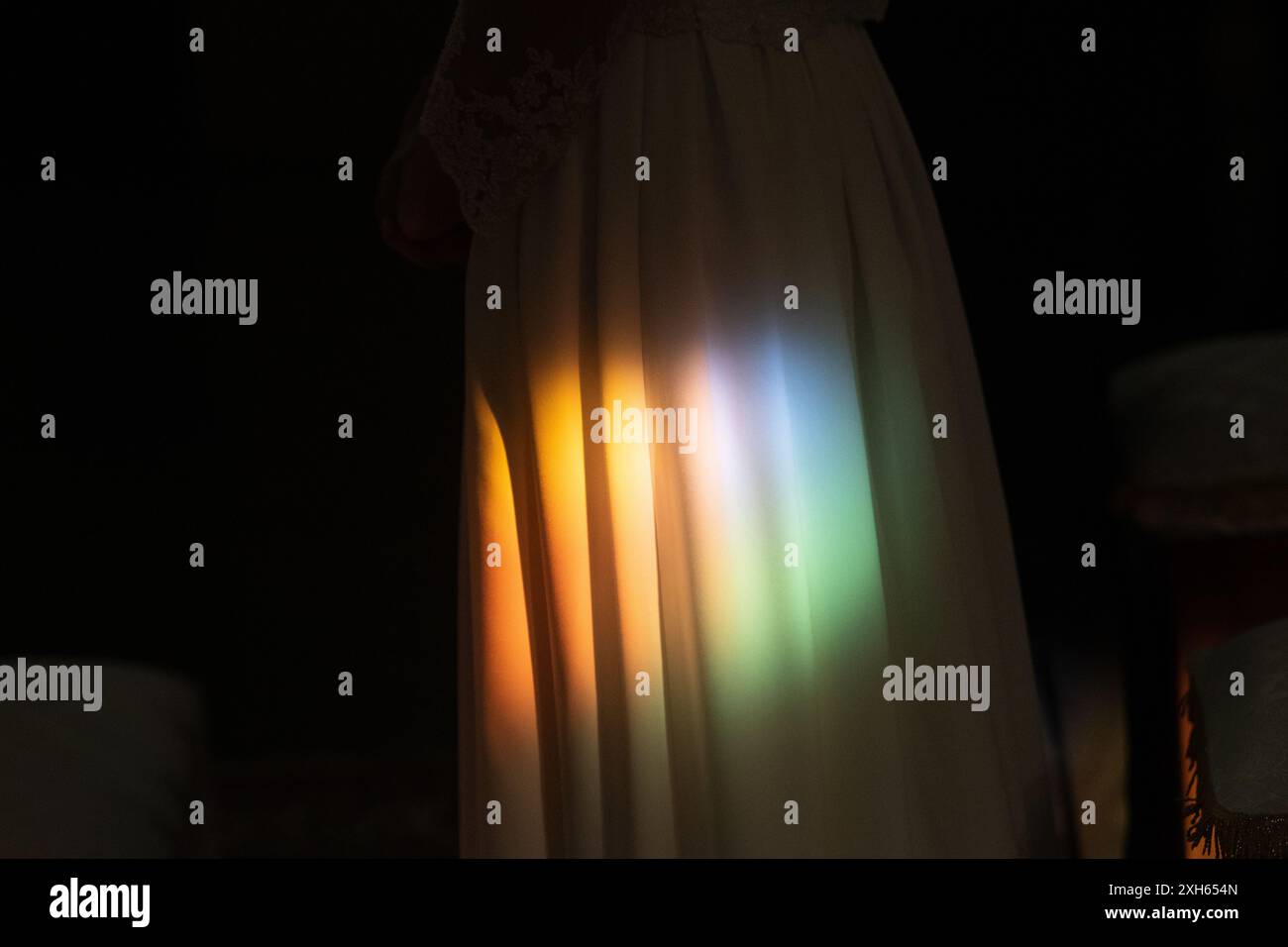 Bride is posing with rainbow light shining on her dress from a stained ...