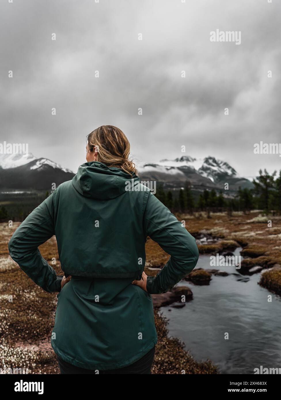 Female wanderlust hiker stands with her hands on her hips, looking out ...