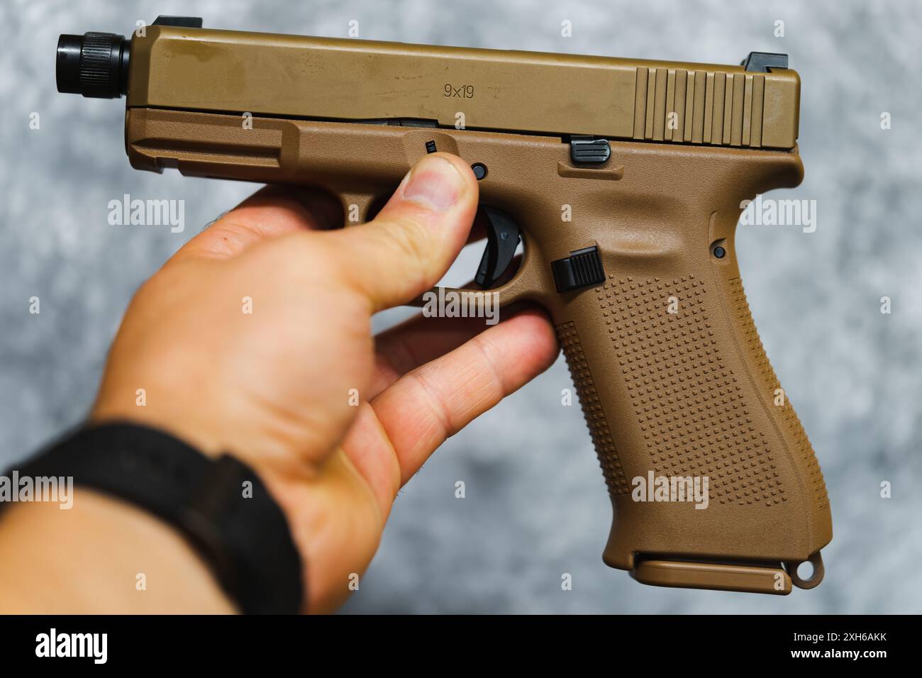 A 9mm sand-colored pistol with a thread for a silencer in a man’s hand ...