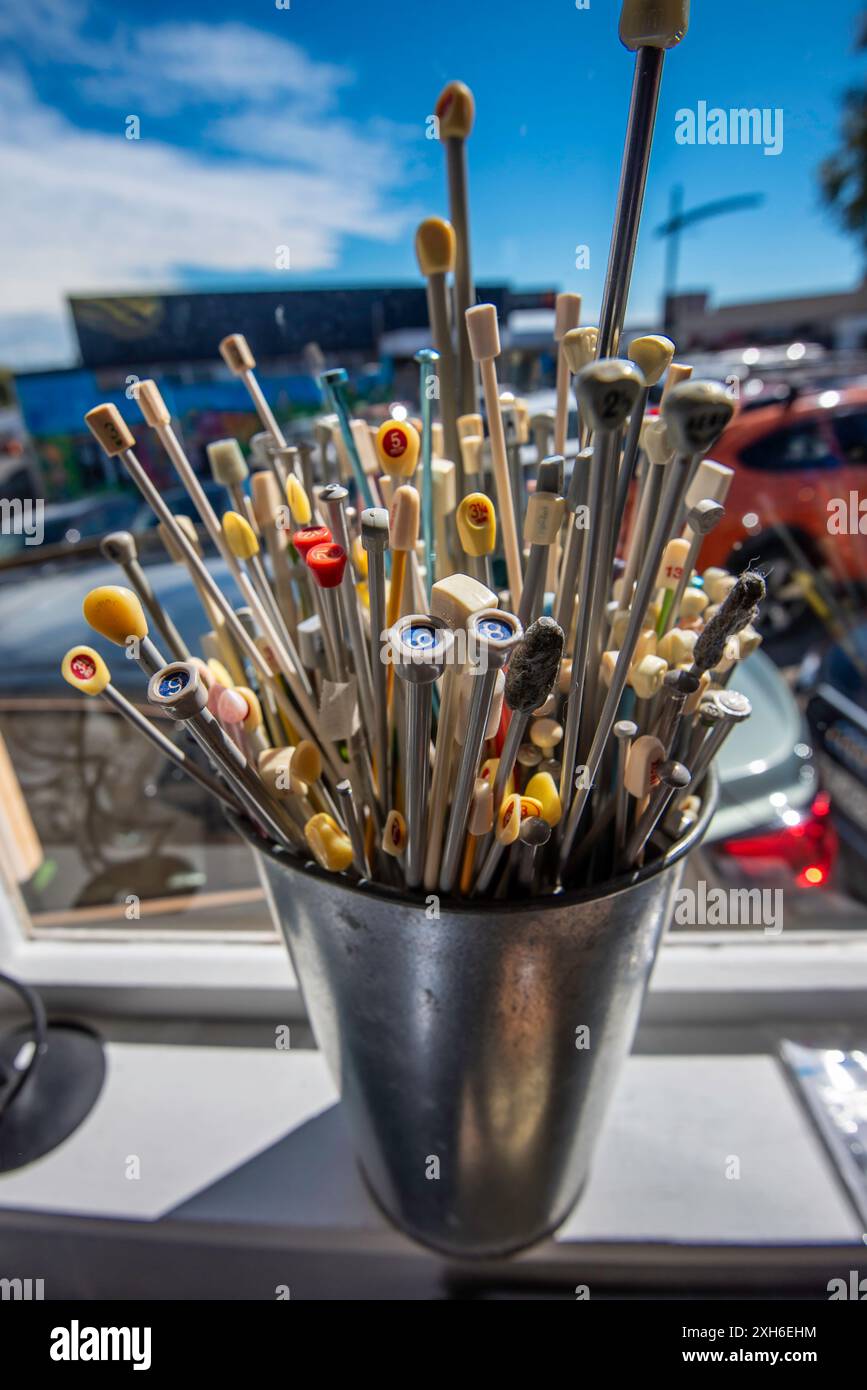 A collection of knitting needles standing upright in a metal container ...