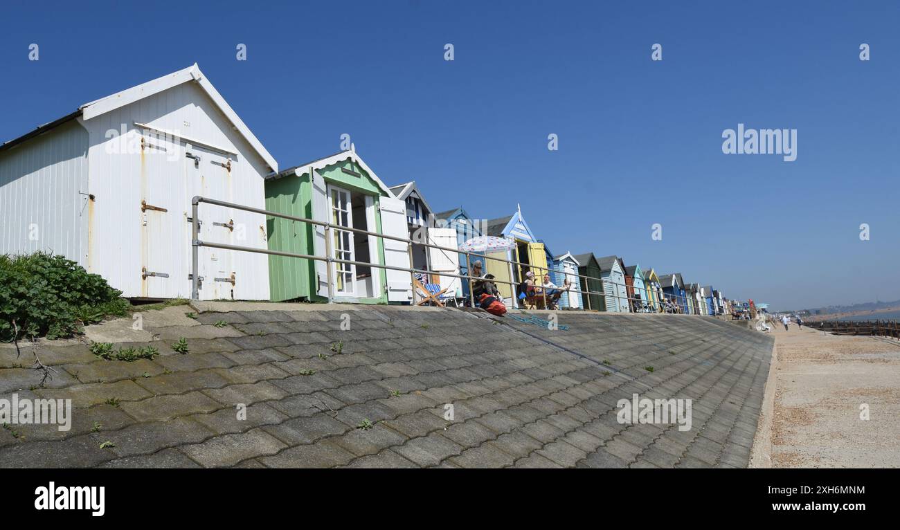 Beach huts on elevated promenade with holiday makers enjoying sunshine ...