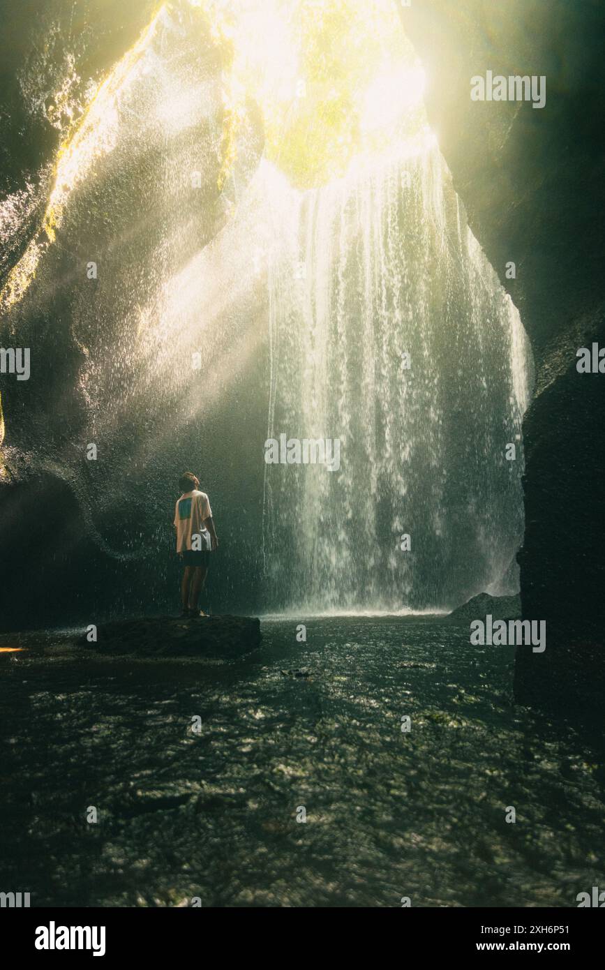 A person standing in front of a waterfall inside a cave with sunlight ...