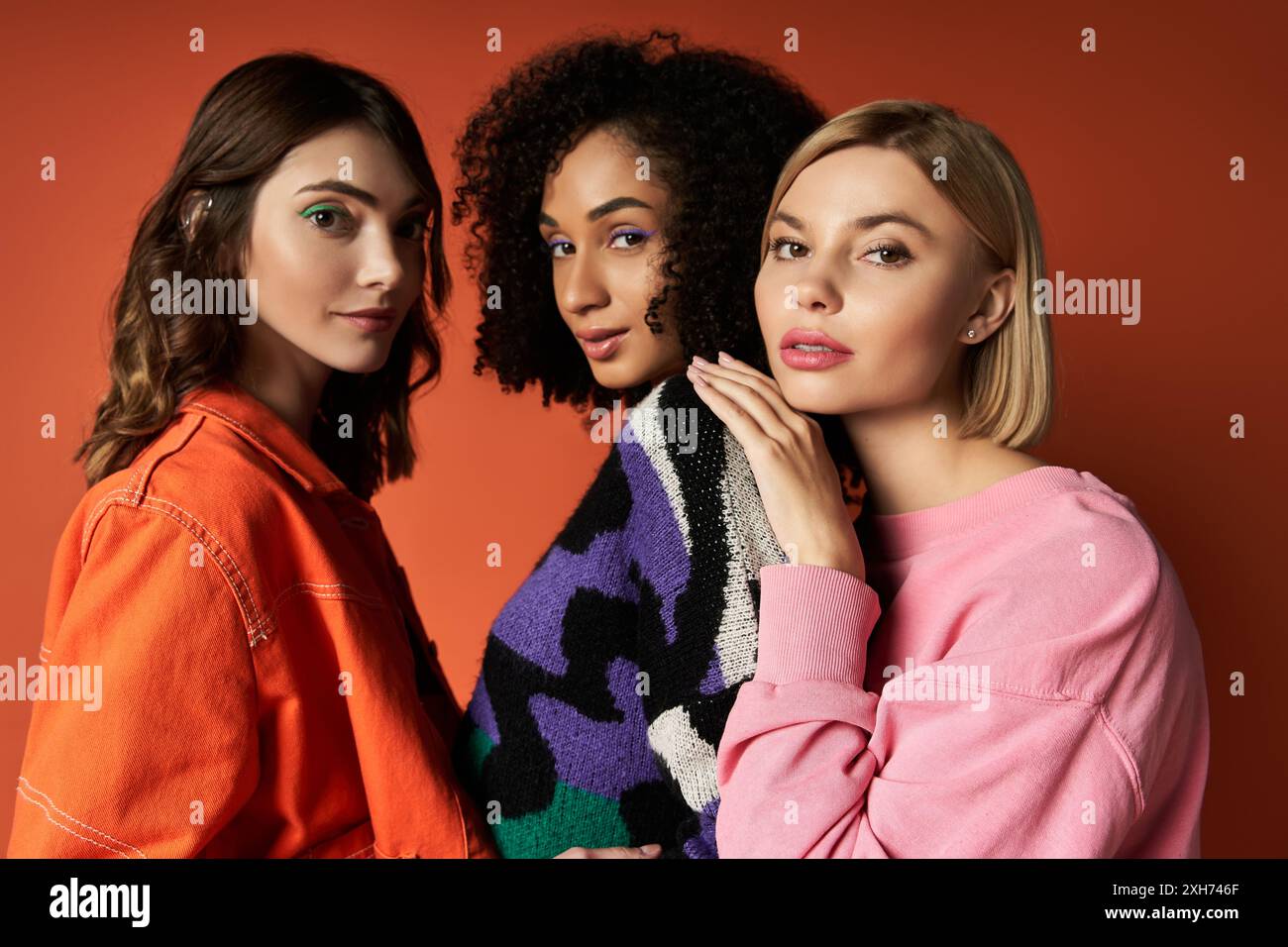 Three young, multicultural women stand stylishly before a vibrant red ...