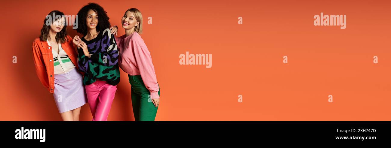 Multicultural women in stylish attire stand together on an orange ...