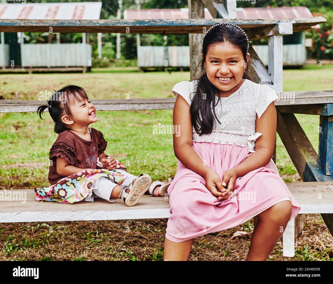 Young indigenous girl and her baby sister sitting on a bench and ...