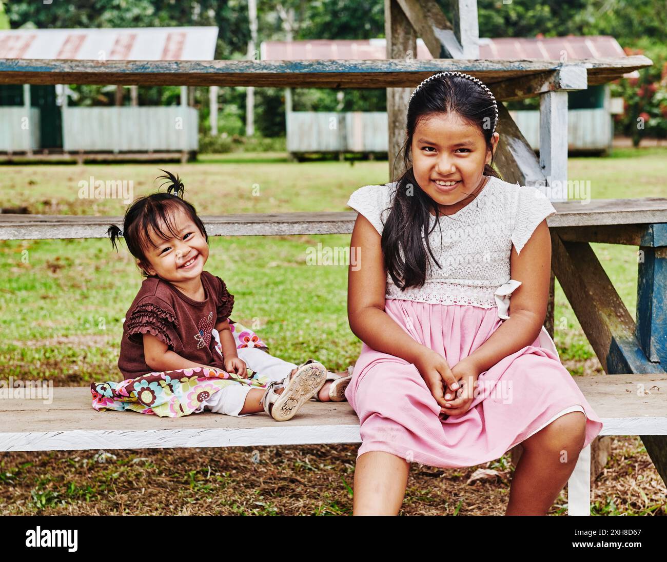 Young indigenous girl and her baby sister sitting on a bench and ...