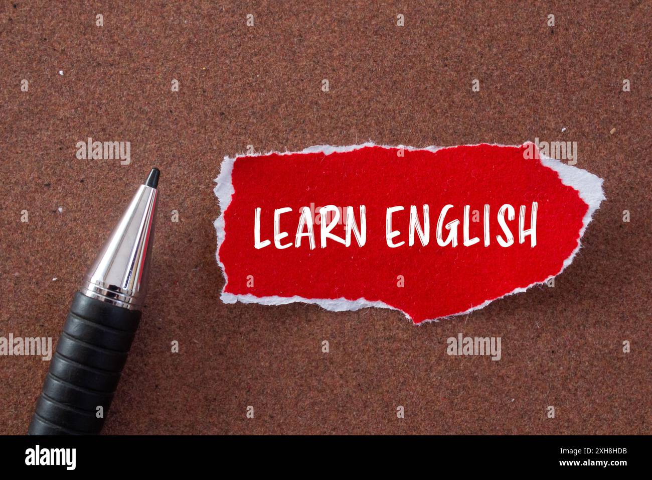 Learn english message written on ripped torn red paper and a pen with brown background ...