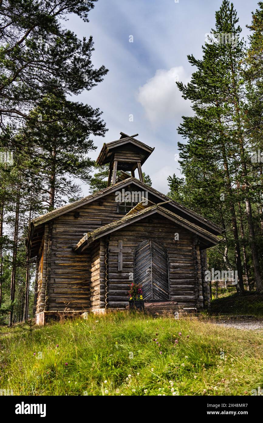 A small wooden mountain chapel stands amidst tall pine trees in the ...