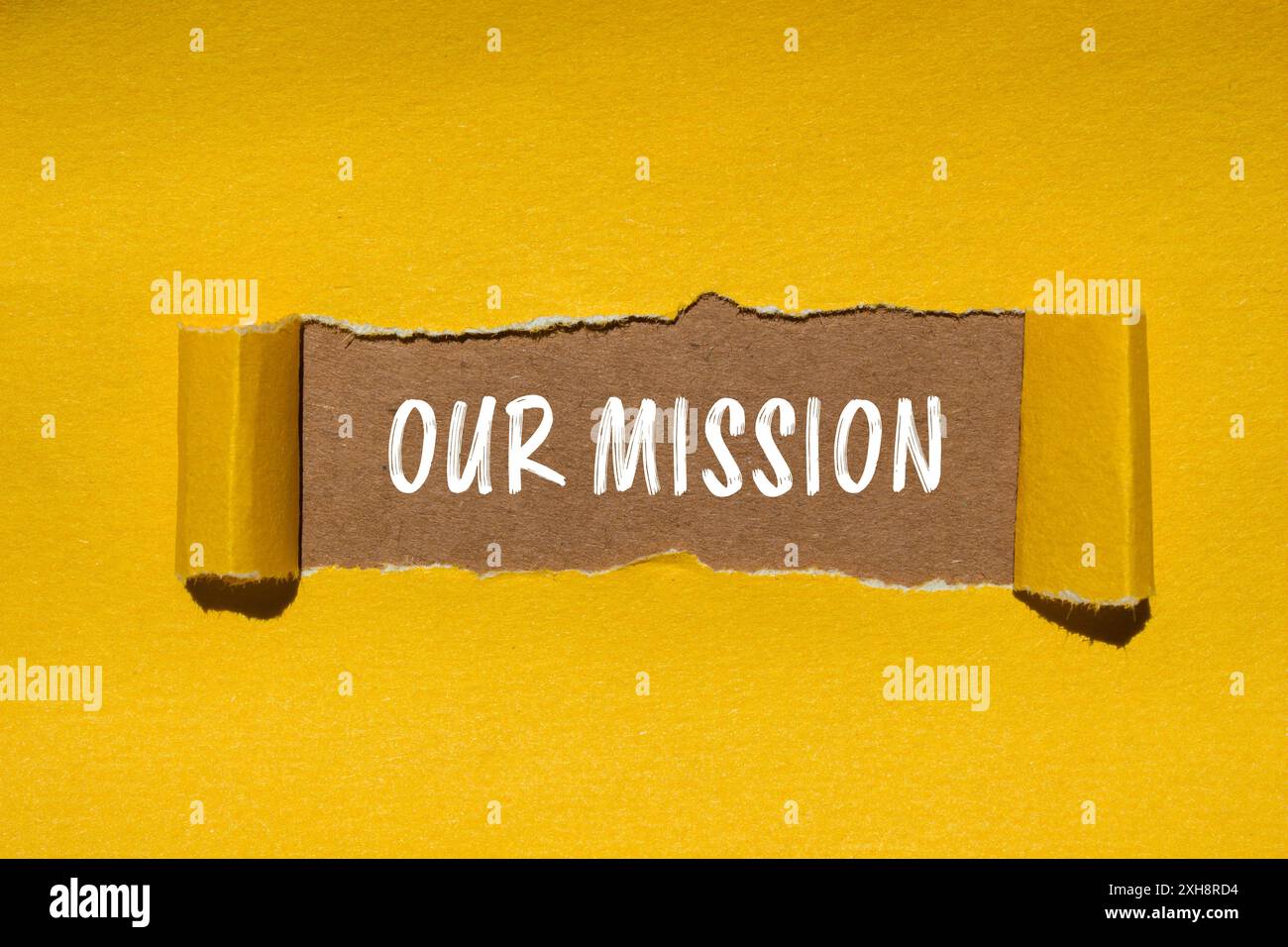 Our mission message written on ripped torn yellow paper with brown background. Conceptual our ...