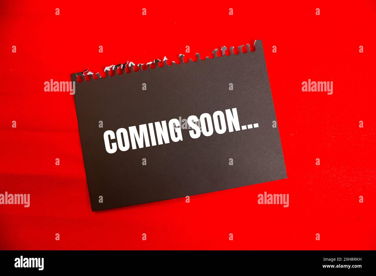 Coming soon message written on ripped black paper piece with red ...