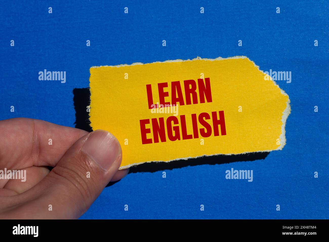 Learn english message written on ripped torn yellow paper with blue background. Conceptual learn ...