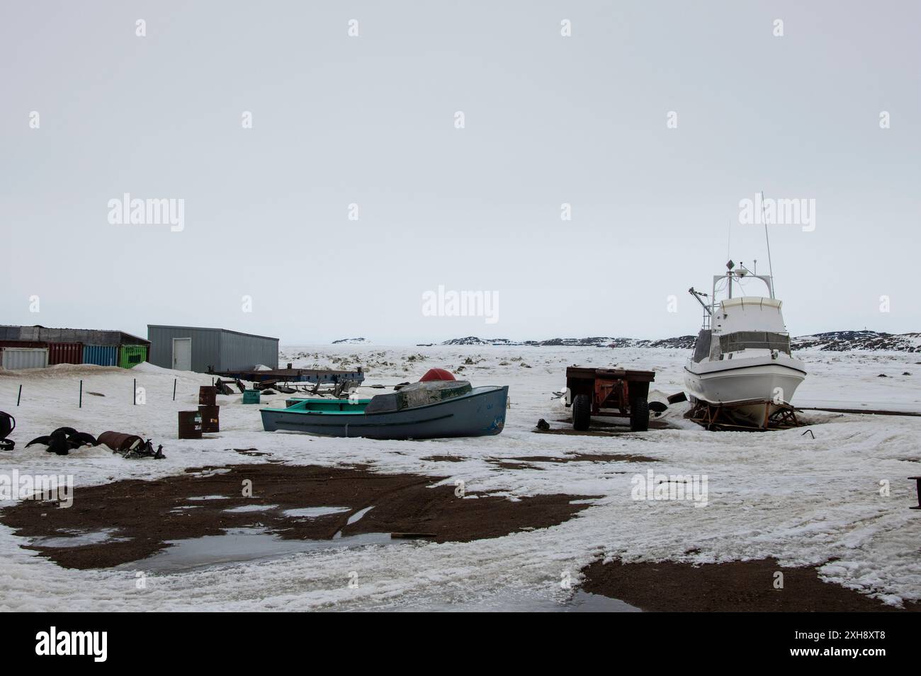 Wooden green boat, a steel barge and white boat stored beach on Frobisher Bay in Iqaluit ...
