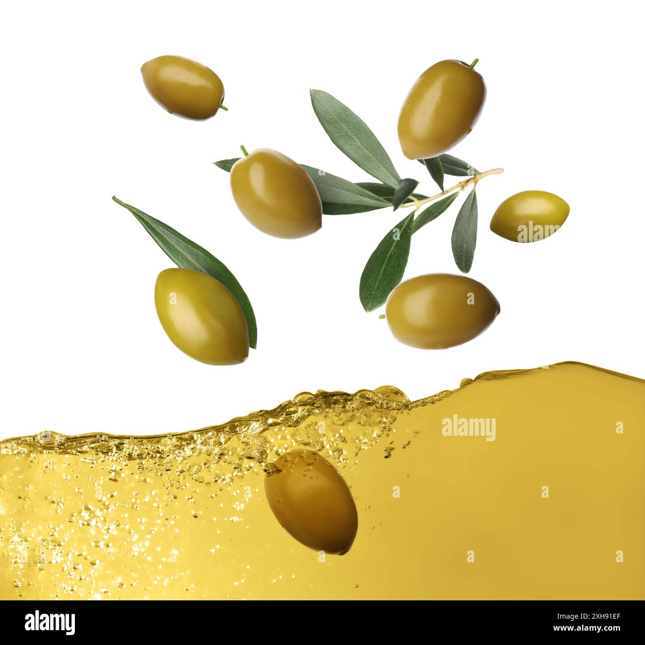 Green olives and leaves falling into cooking oil on white background ...