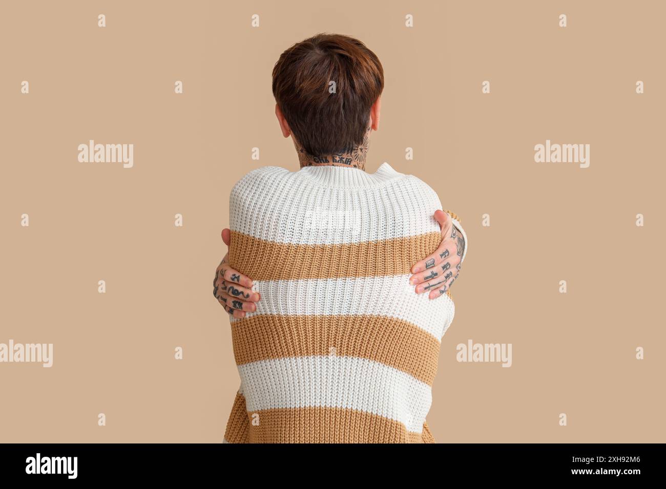 Young man hugging himself on beige background, back view Stock Photo ...