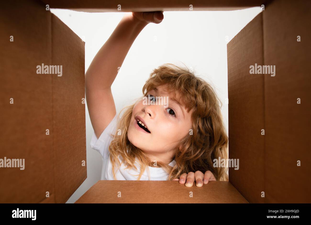 Kid unpacking and opening carton box, and looking inside with surprise ...