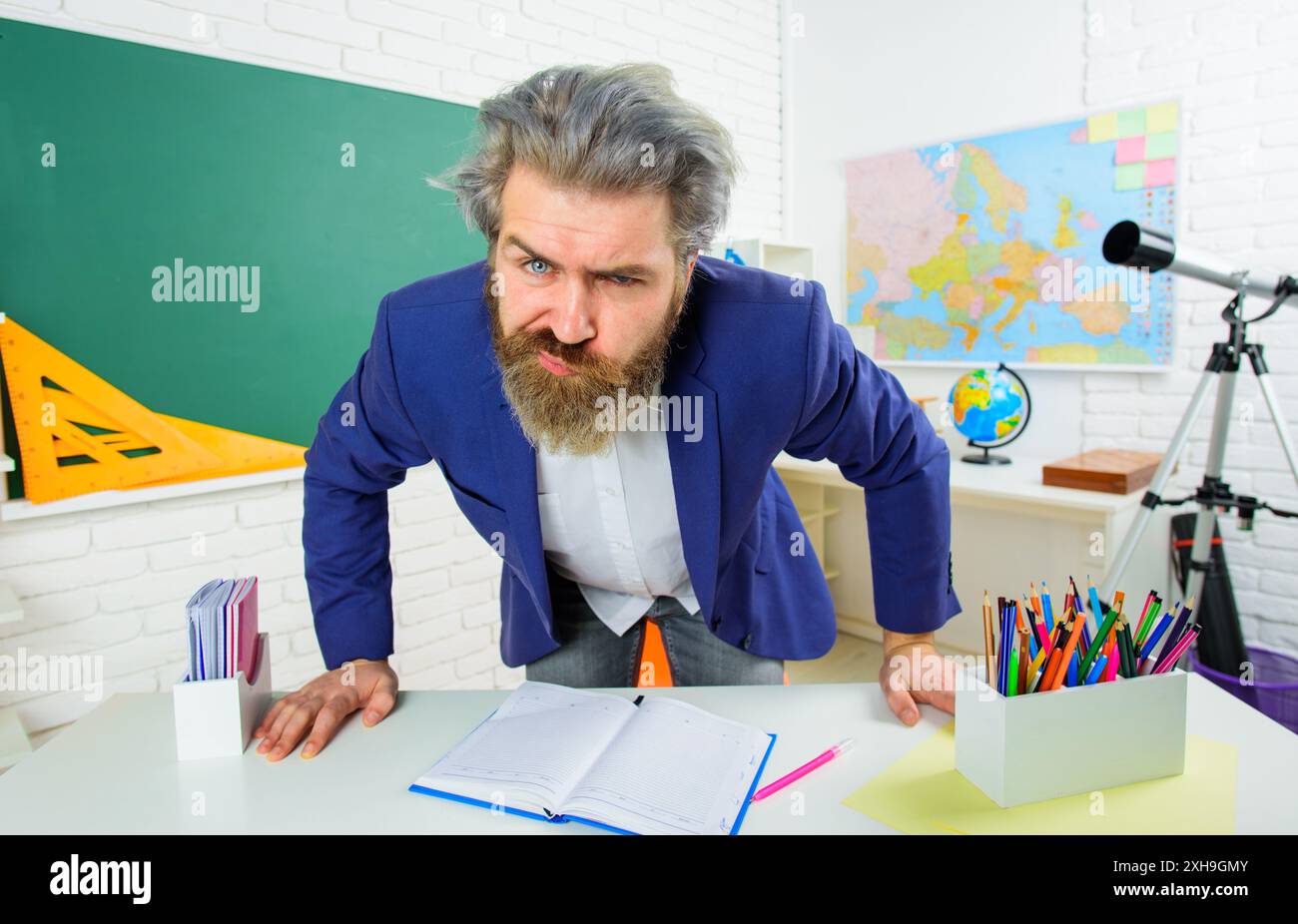 Angry male school teacher at desk in university. Bearded man in suit ...
