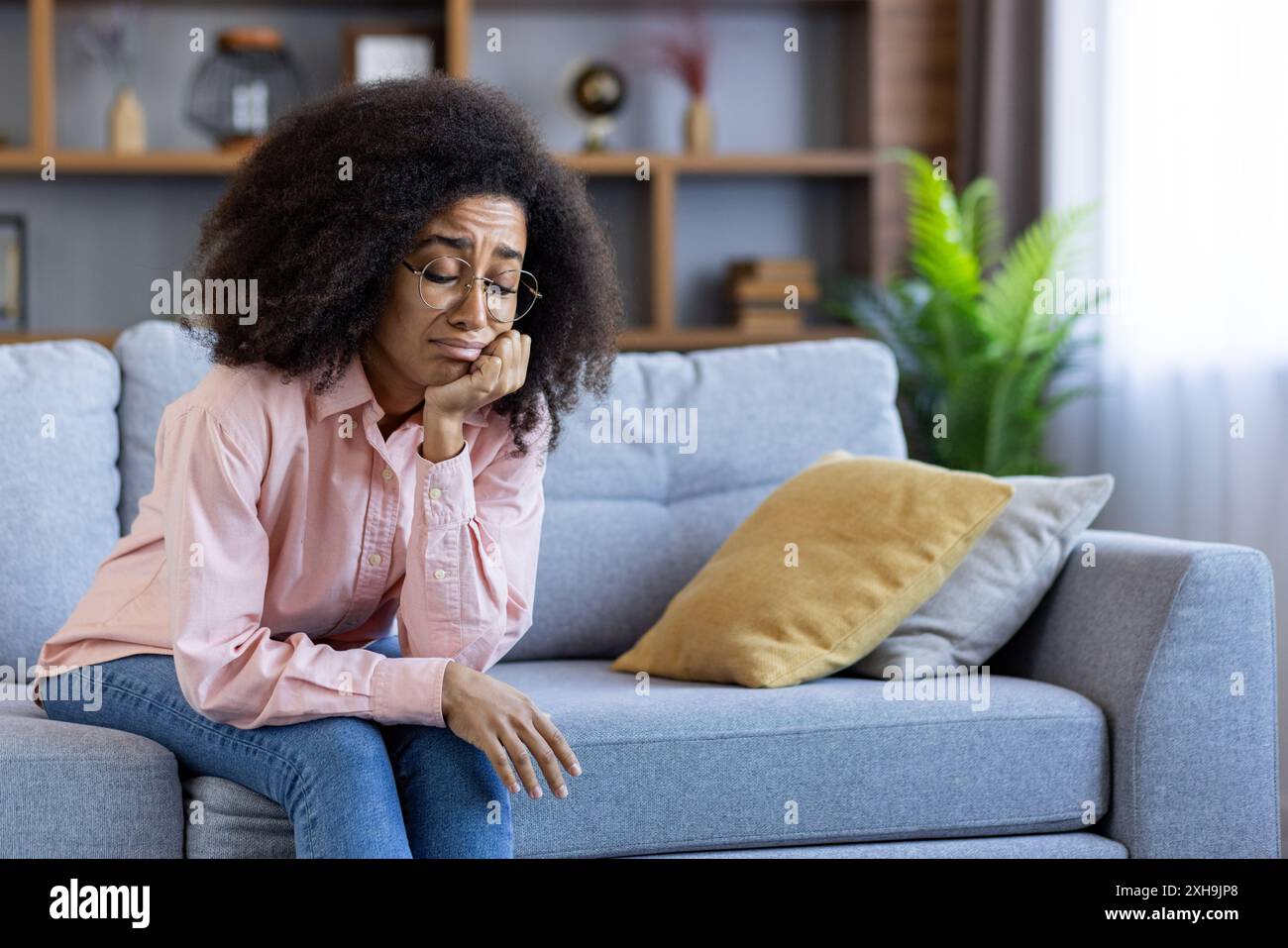 Woman looking sad and reflective sitting on couch in modern living room ...