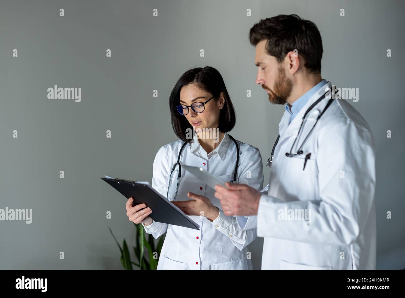 Doctors reviewing patient information on digital tablet and clipboard. Medical professionals ...