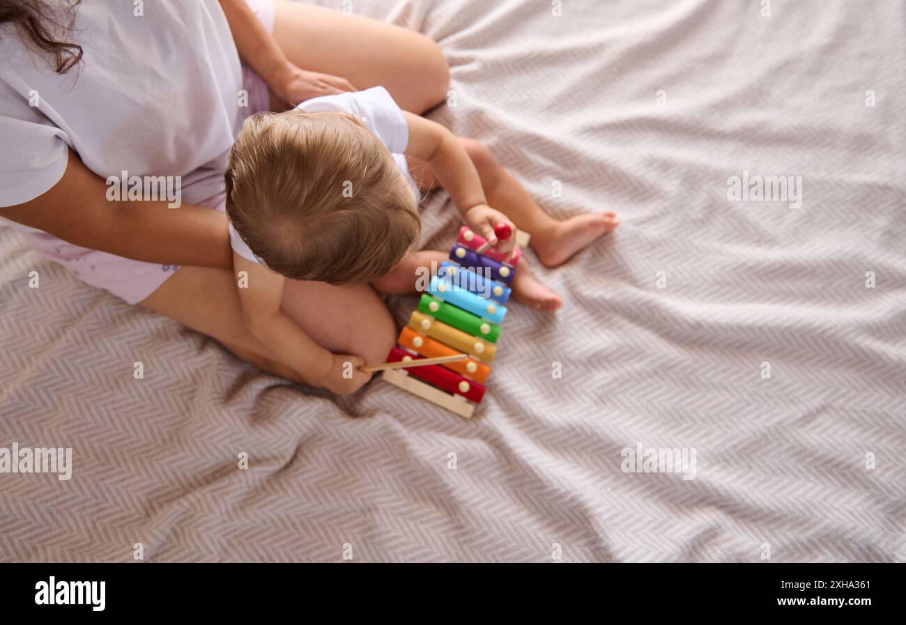 Mother and toddler on a bed playing with a colorful xylophone. The scene depicts bonding ...