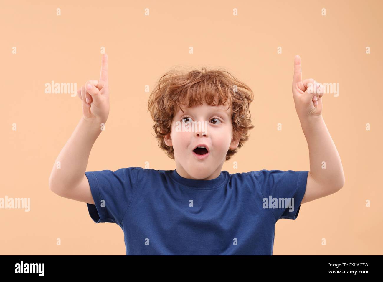 Portrait of emotional little boy pointing at something on beige ...