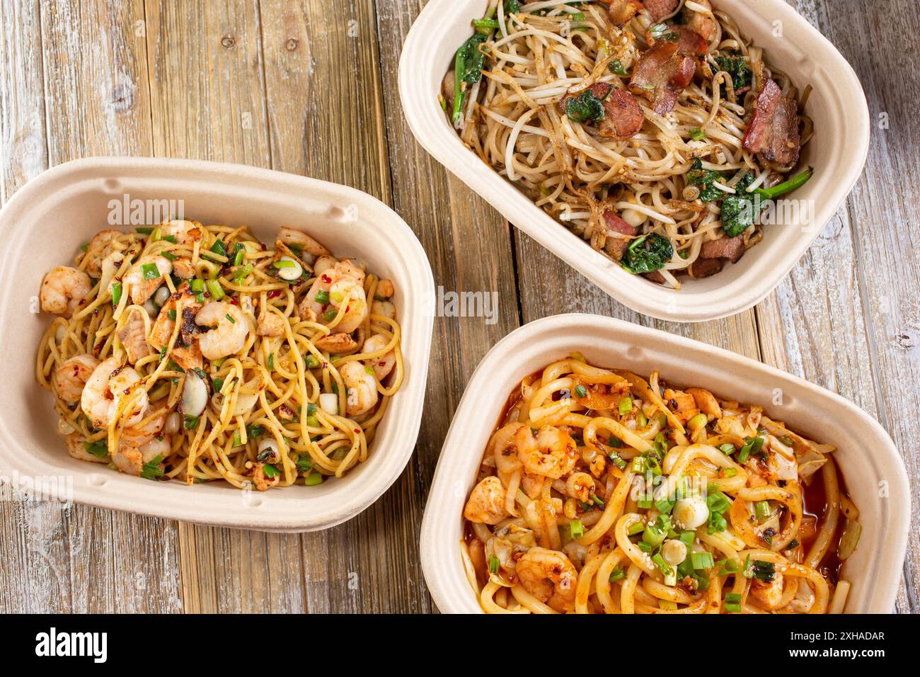A top down view of several paper bowls of pan Asian noodle entrees ...