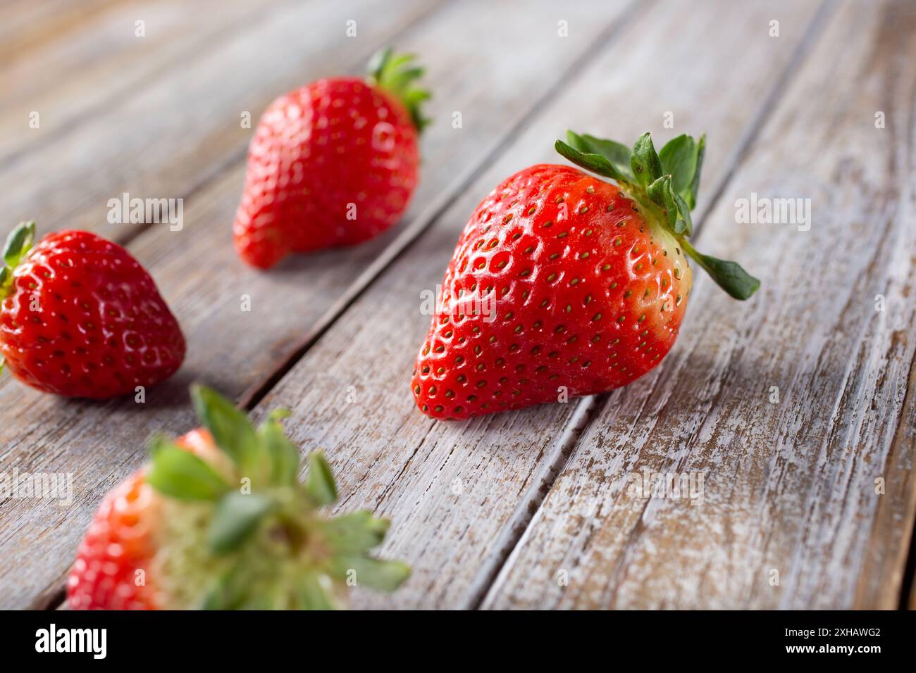 A view of several strawberries scattered around a wood table surface ...
