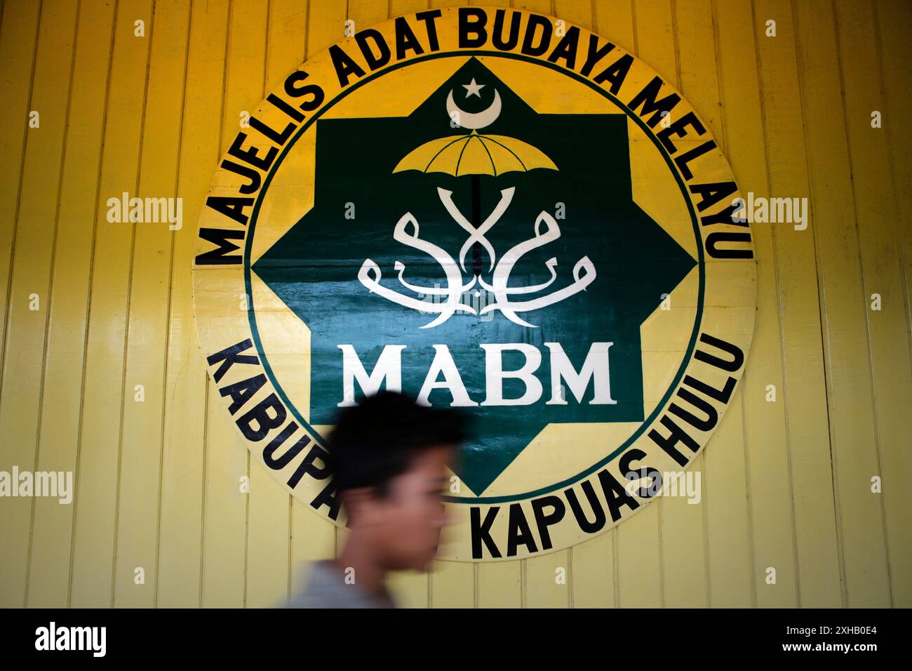 A young man walks past the logo of Majelis Adat Budaya Melayu ...
