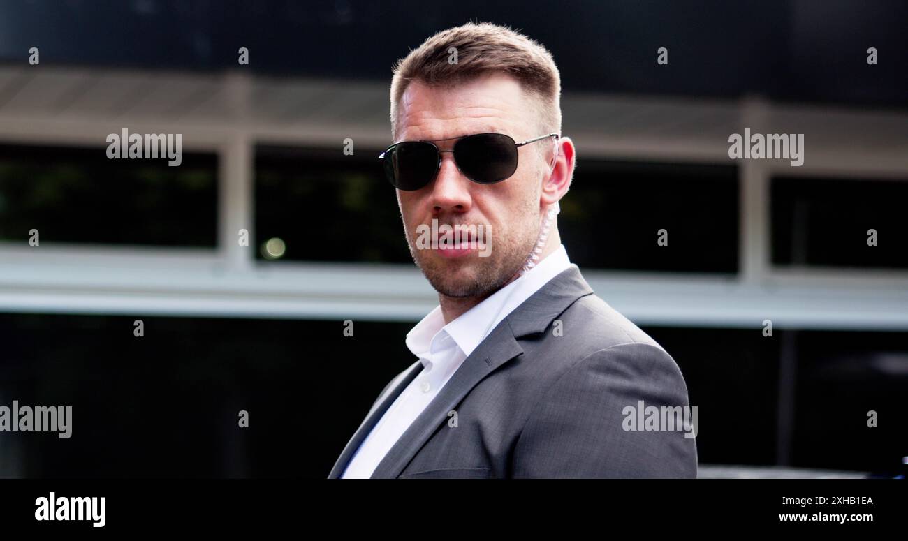 Strong security guard in sunglasses safeguarding entrance with ...