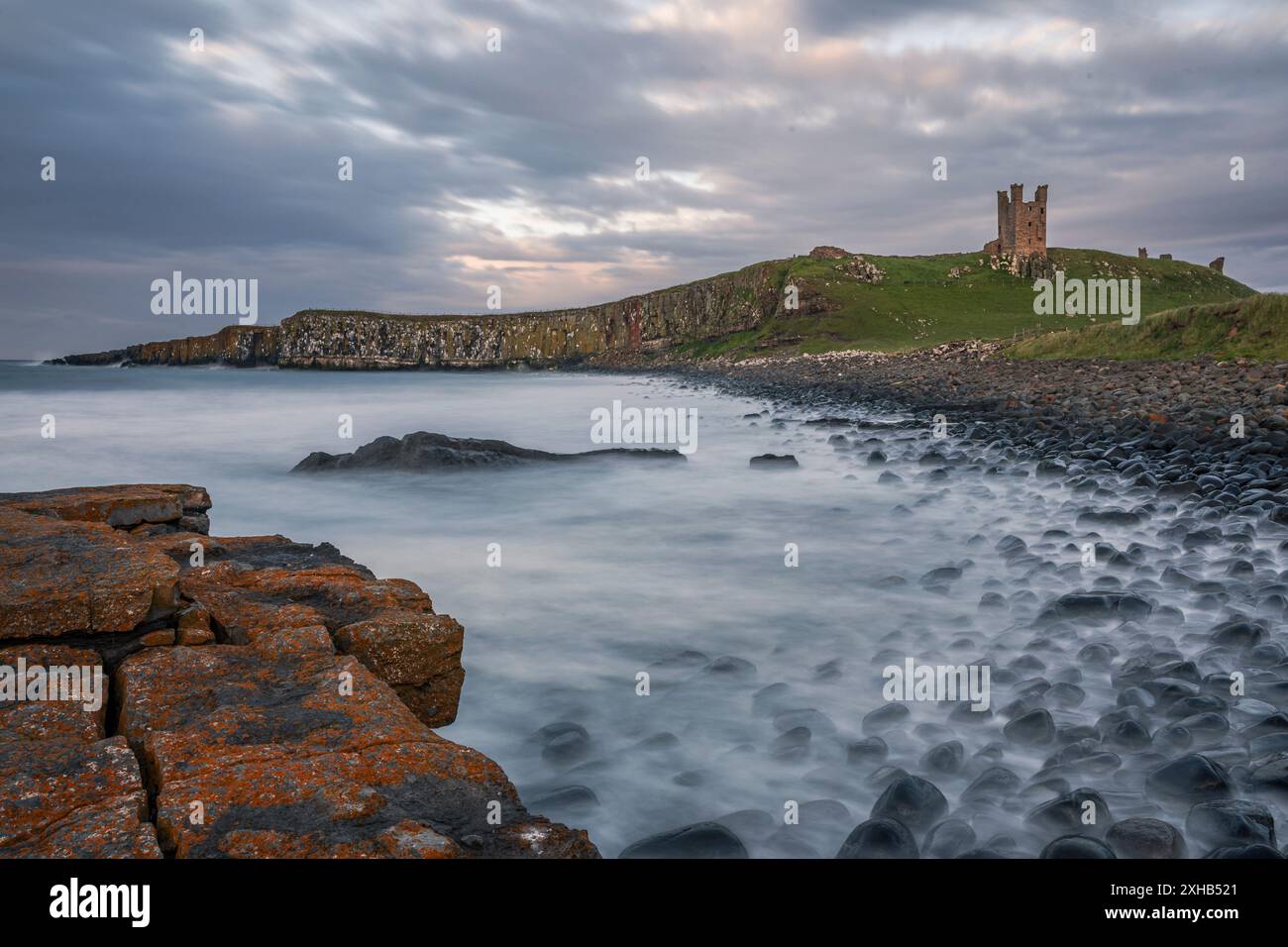 The ruins of Dunstanburgh castle ubove the black rocks of Rumble Churn ...