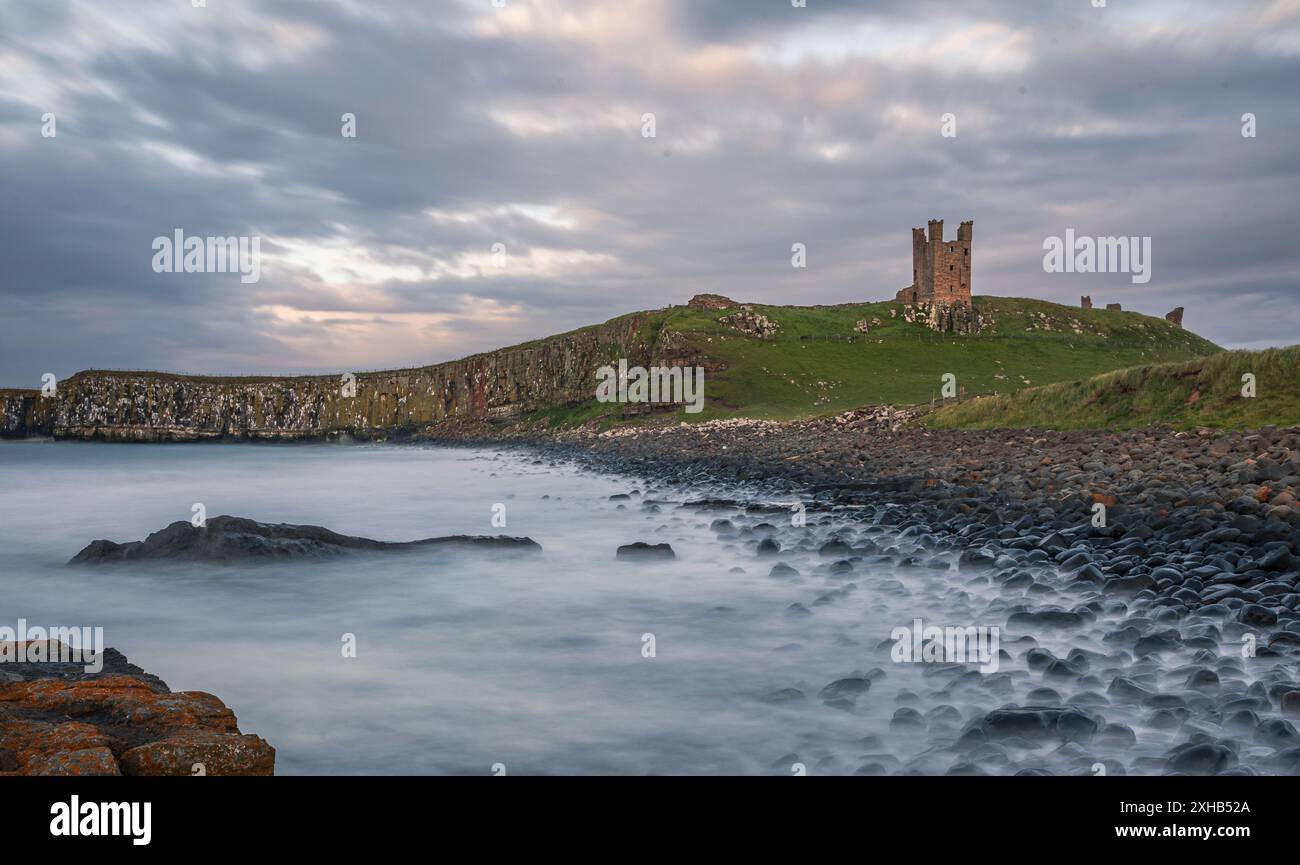 The ruins of Dunstanburgh castle ubove the black rocks of Rumble Churn ...