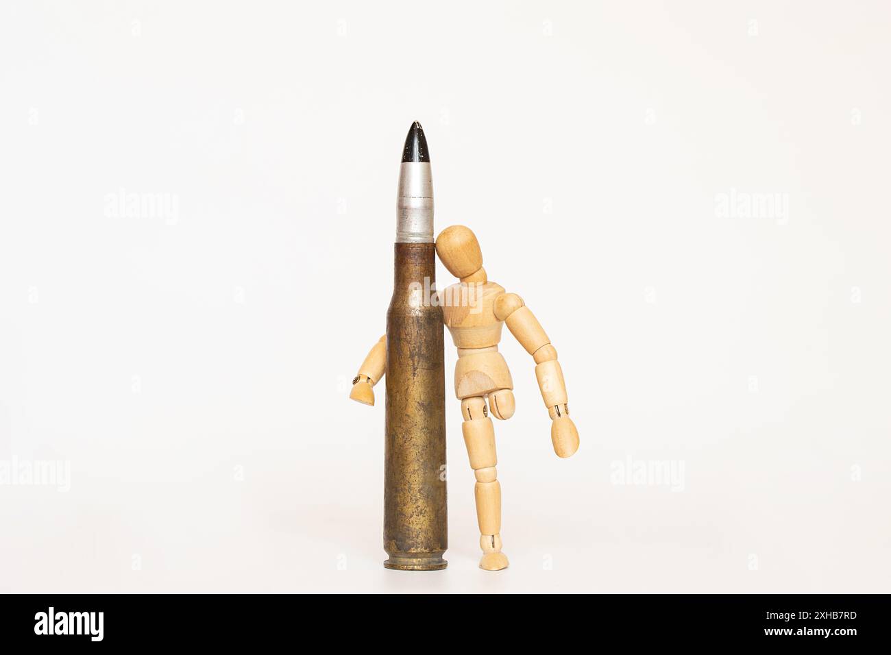 A wooden man stands on one leg and holds on to a bullet on a white ...