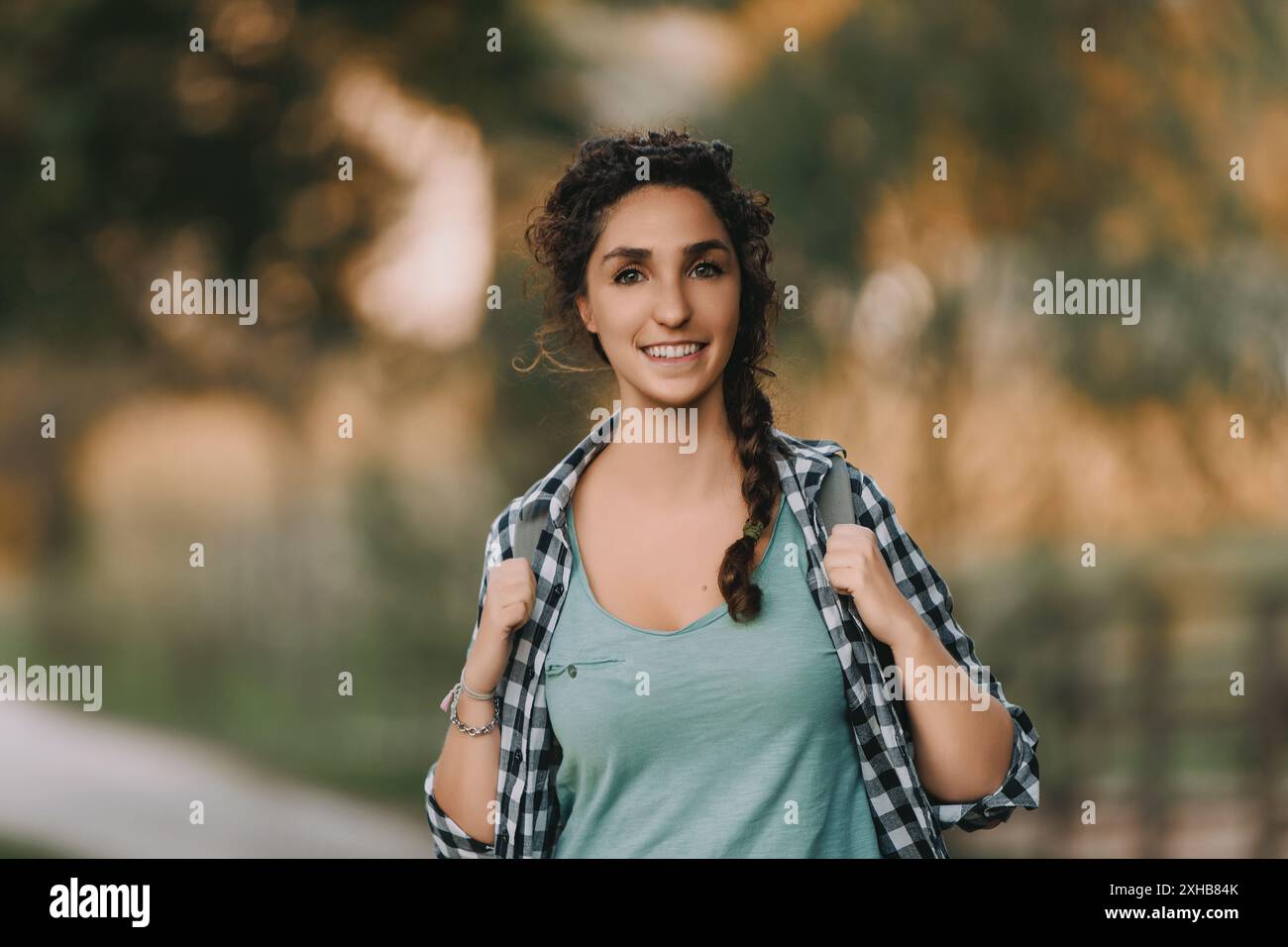 Young woman with curly braided hair and a checkered shirt smiles ...