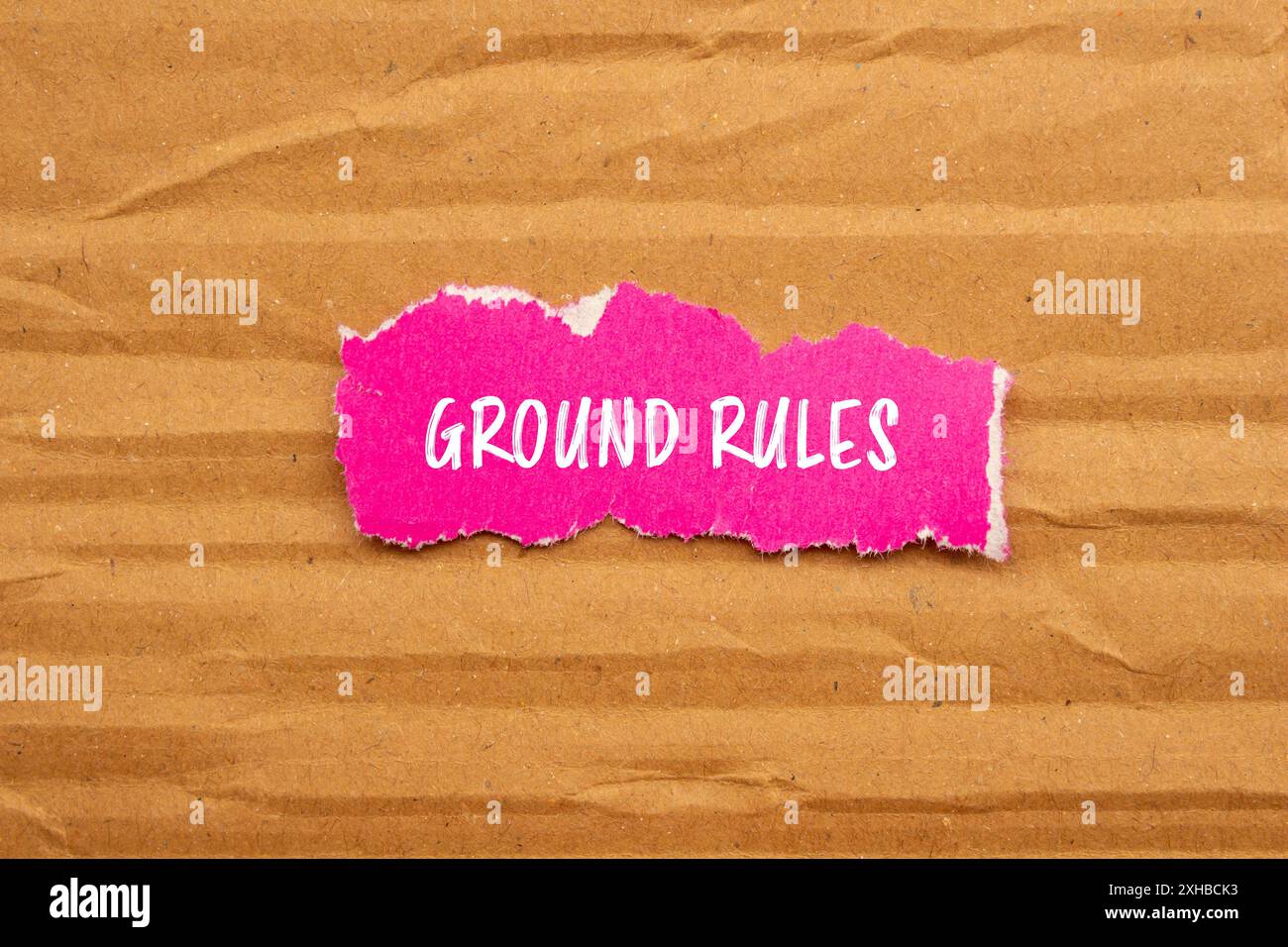 Ground rules message written on ripped pink paper piece with cardboard background. Conceptual ...