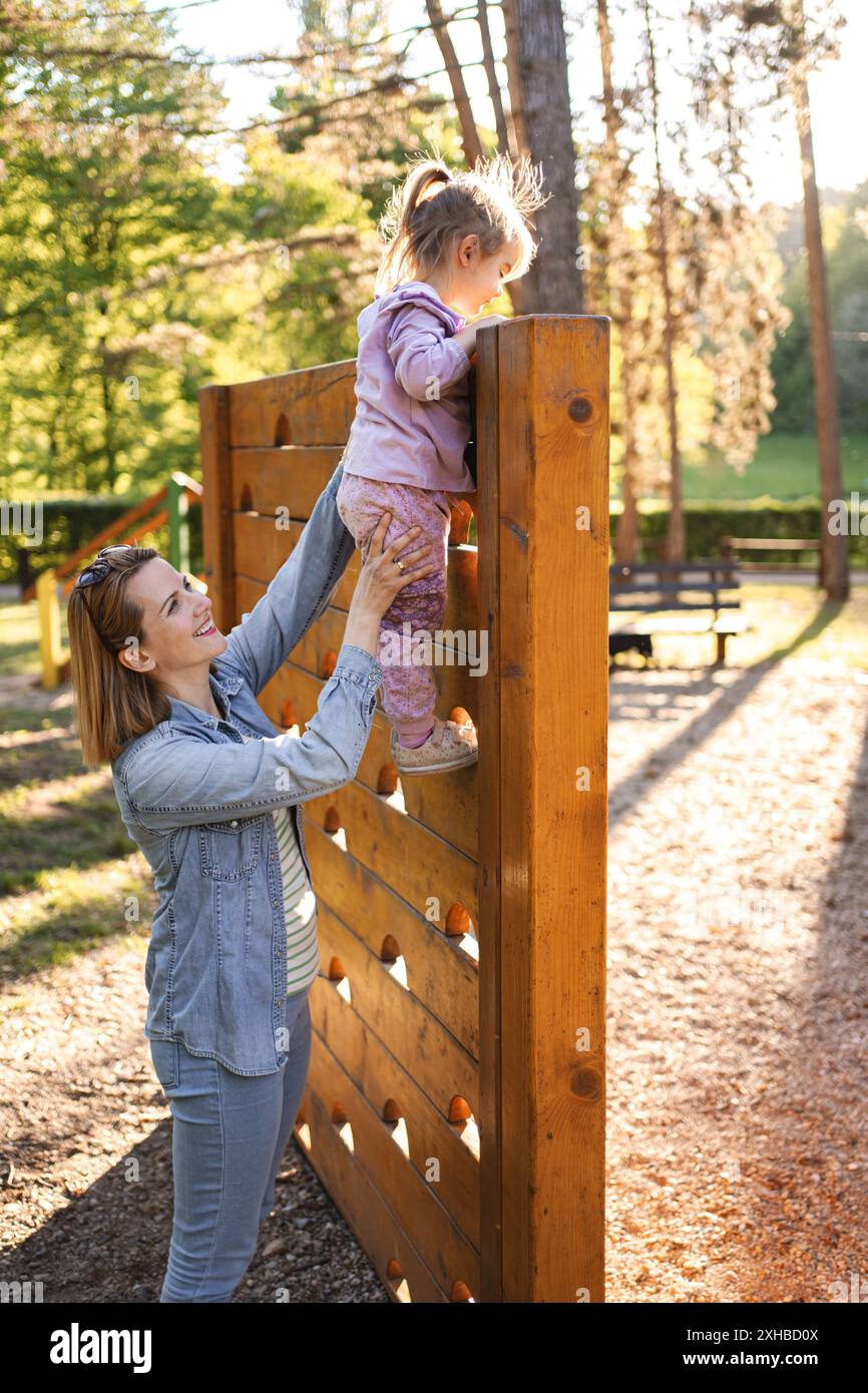 Smiling mom helps her cute daughter climb the playground Stock Photo ...