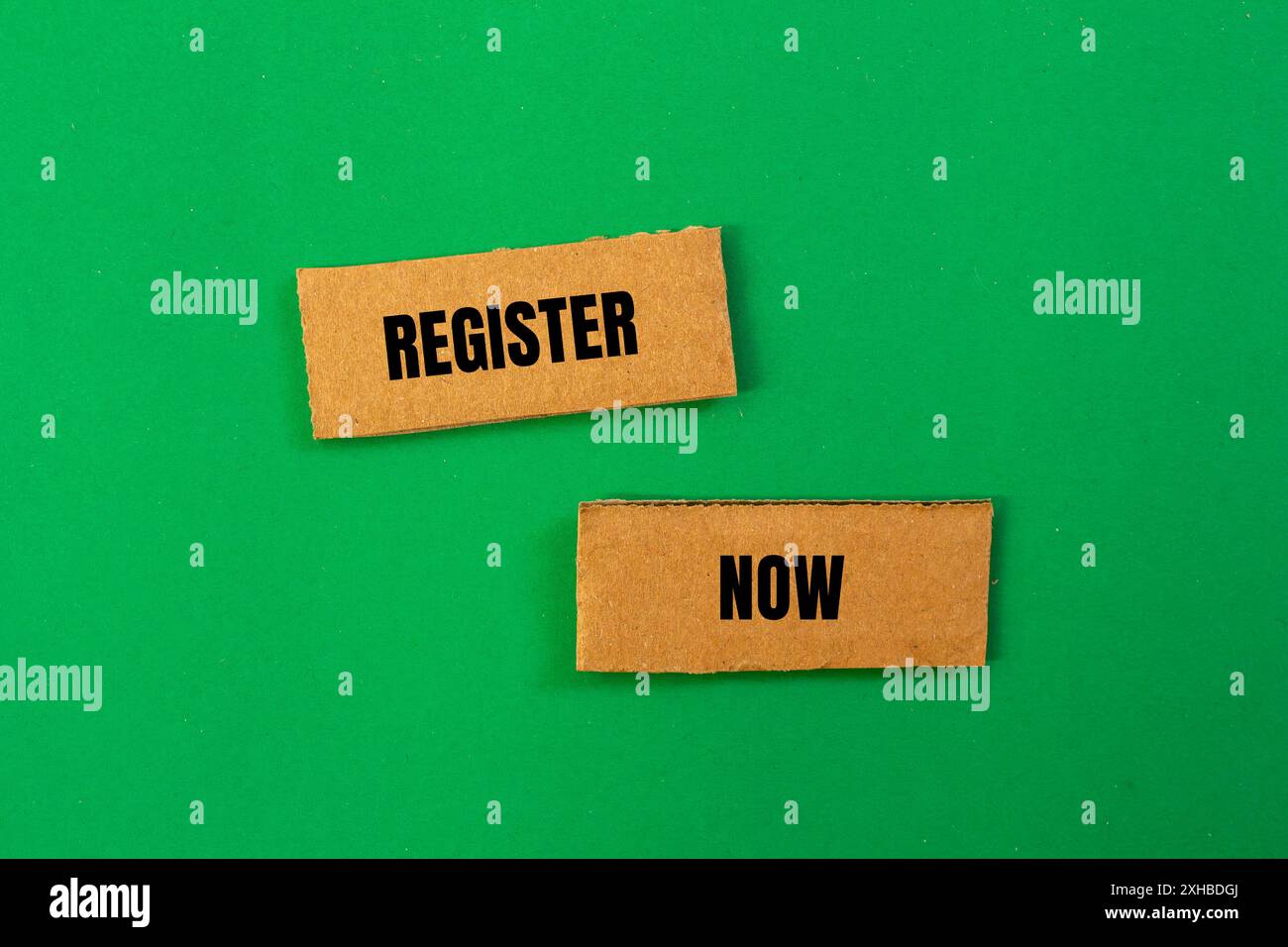 Register now message written on ripped cardboard paper pieces with green background. Conceptual ...