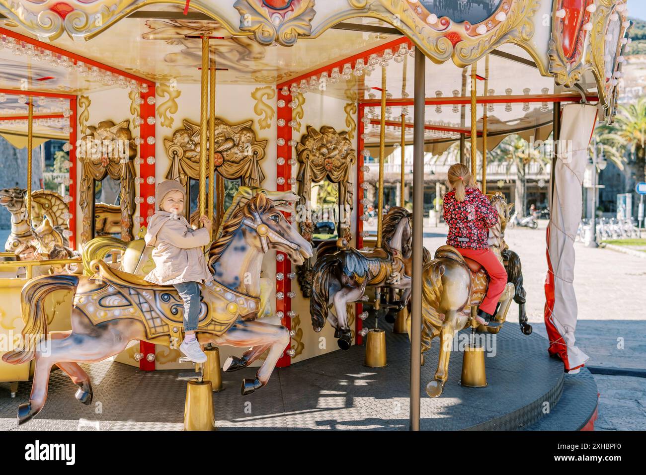 Little girls ride on a colorful carousel holding on to poles. Side view ...