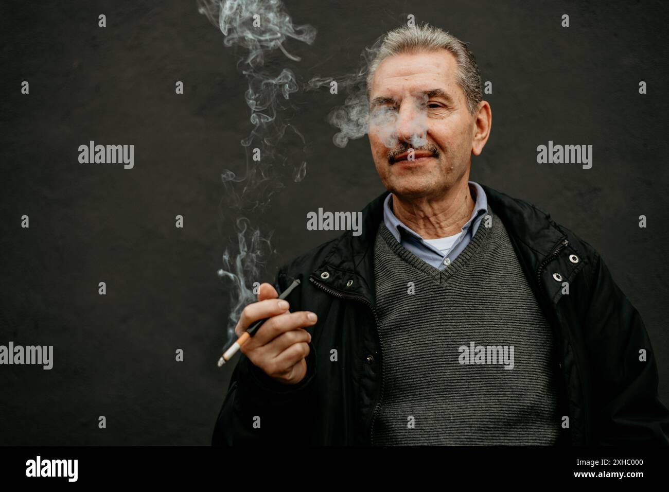An older man with grey hair and a mustache is smoking a cigarette ...