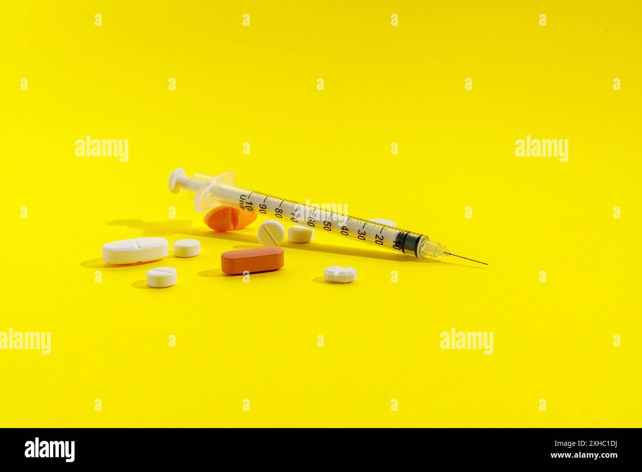 A syringe, several white pills, and one orange and one red pill lie ...