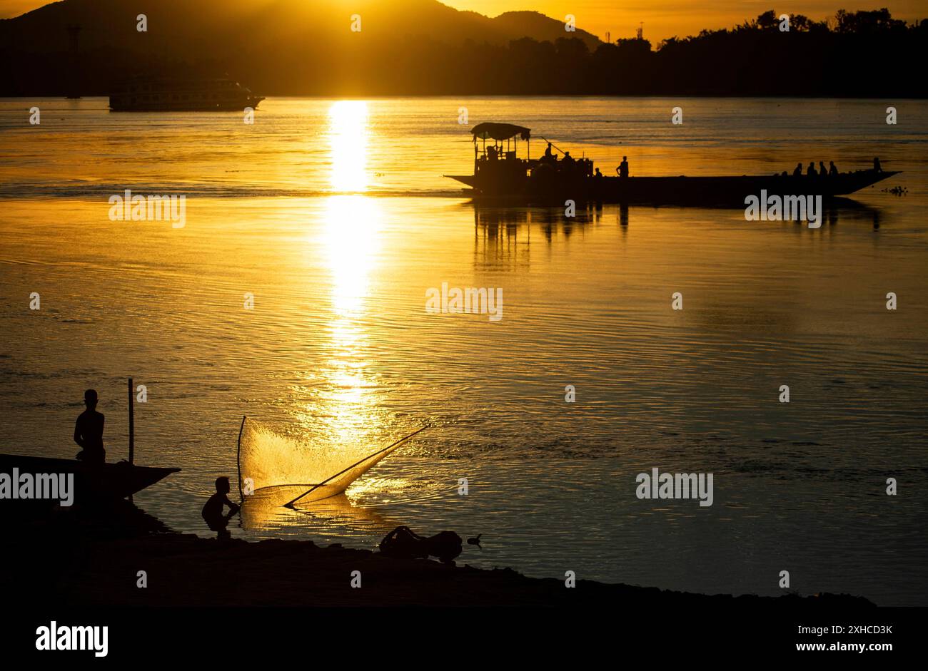Fishermen fishing next to boats in the Brahmaputra river, during sunset ...