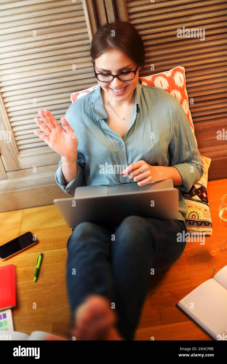From above anonymous woman sitting on floor near glass of wine and open planner and browsing ...
