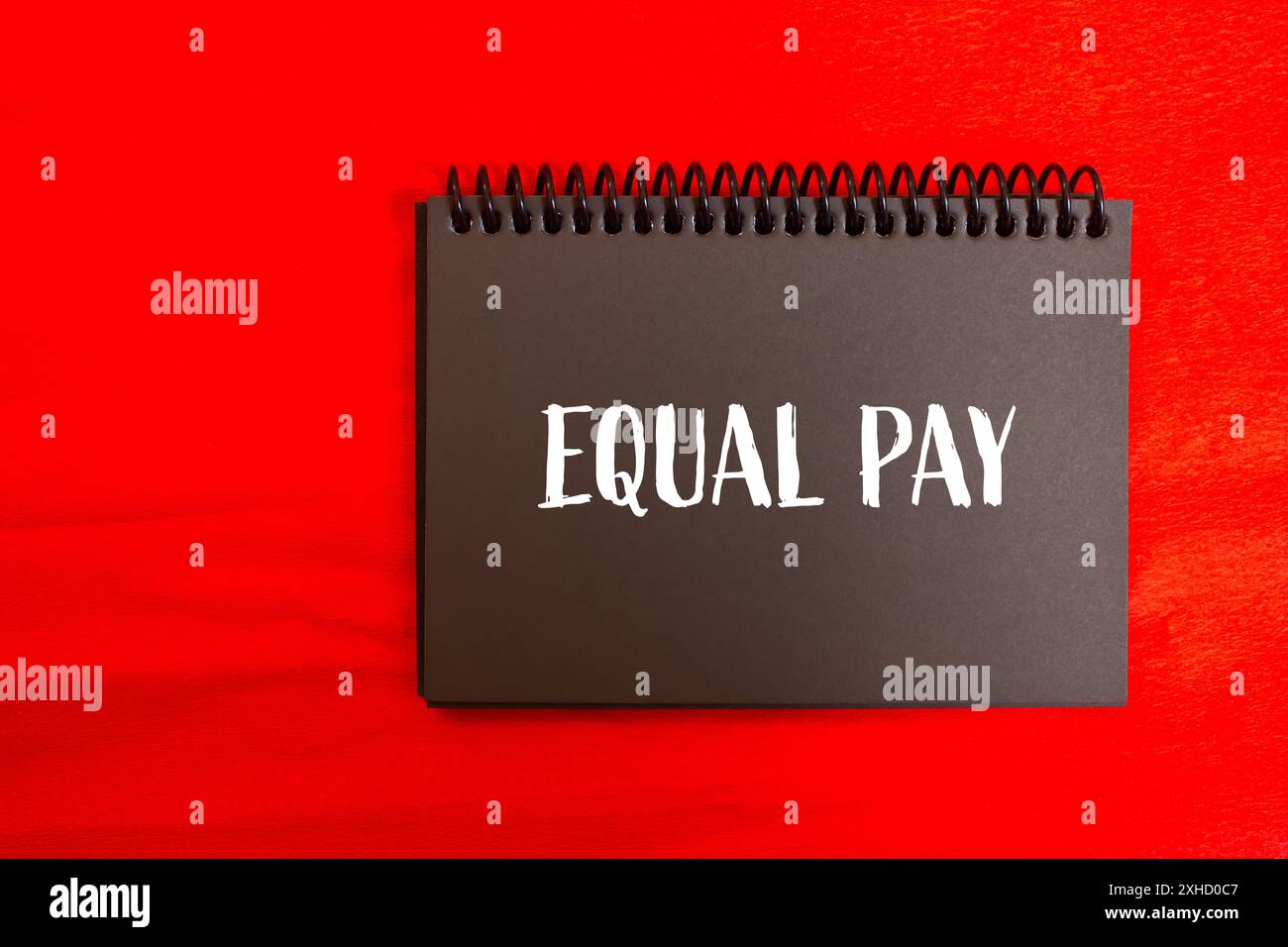 Equal pay message written on black notebook page with red background ...