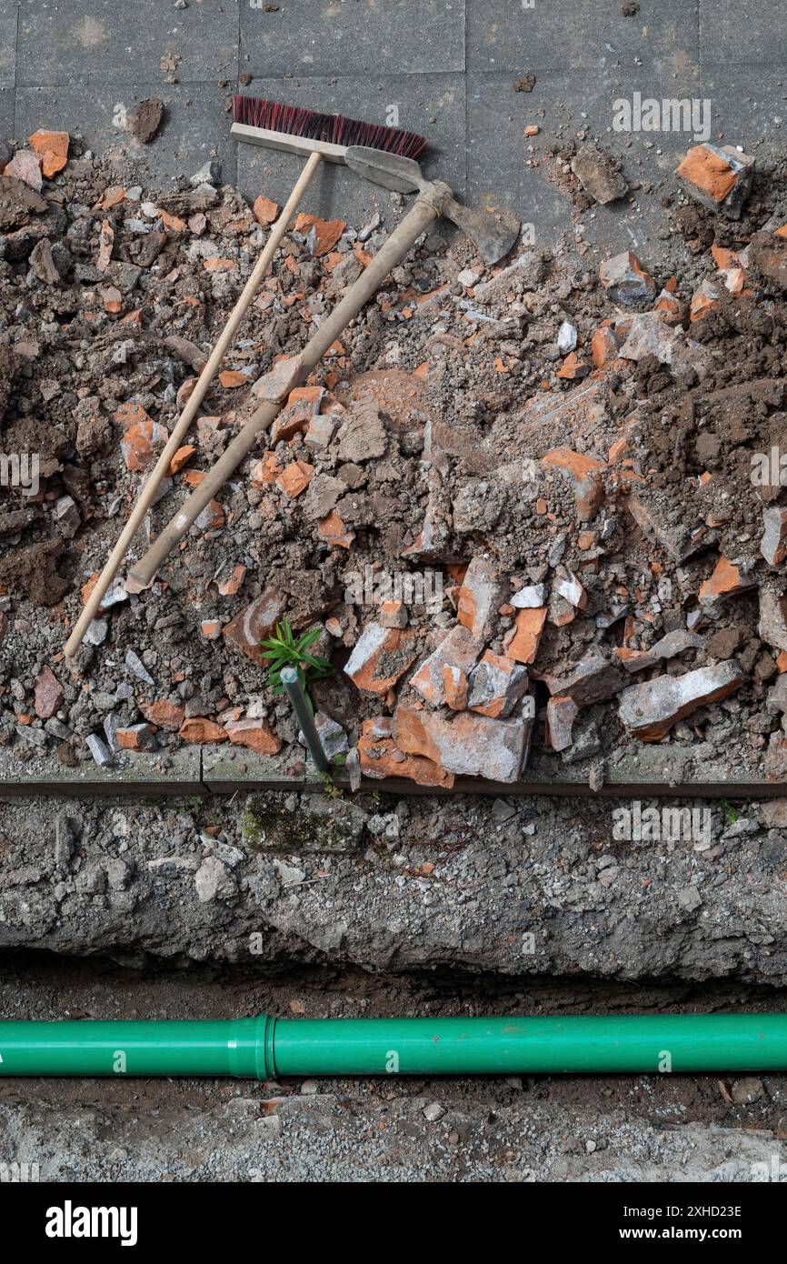 Newly laid green sewage pipe, trench, excavation, broom and pickaxe ...