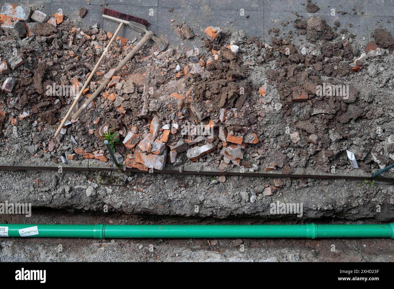 Newly laid green sewage pipe, trench, excavation, broom and pickaxe ...
