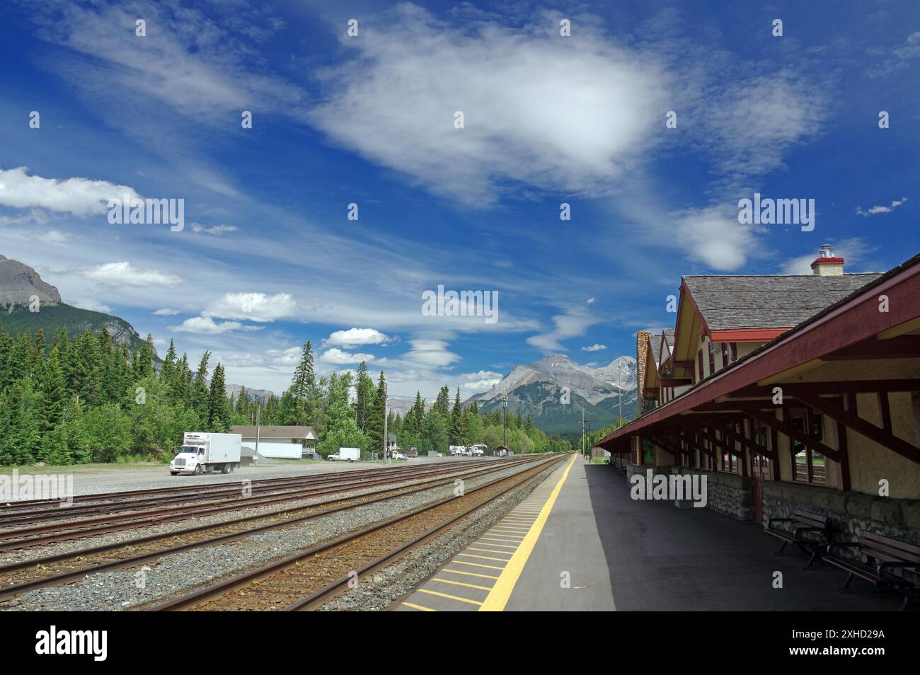 Railway tracks next to a station with mountain landscape and cloudy sky in the background, Banff ...