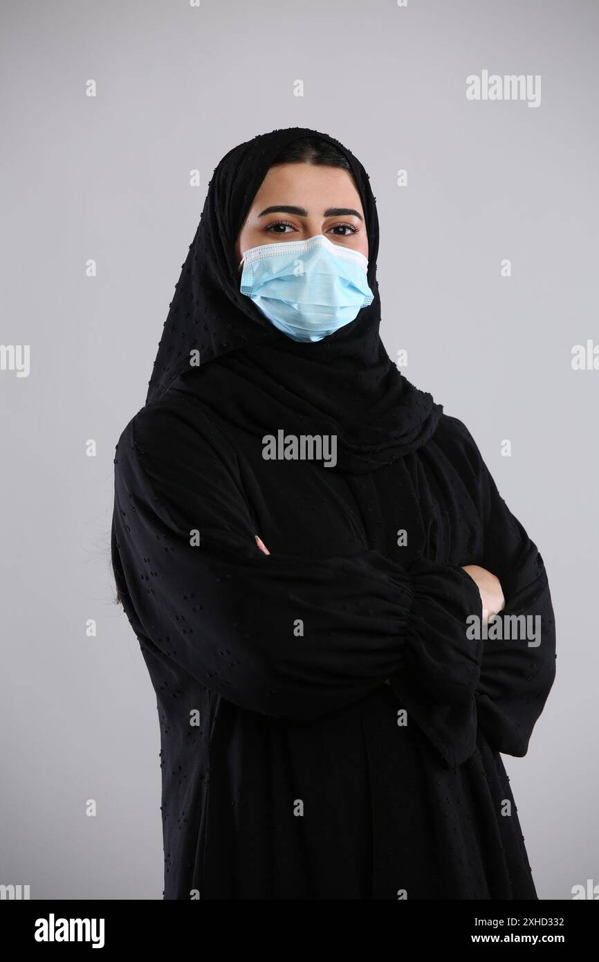 saudi arabian woman lady corssing hands and standing wearing hijaab and mask looking infront ...
