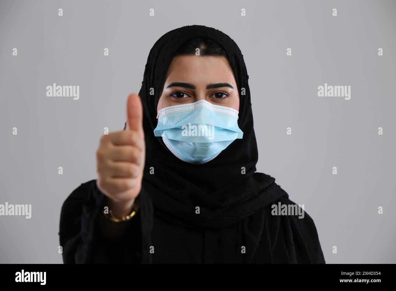 Saudi Arabia Woman in abaya wearing mask standing with thumbs up sign ...