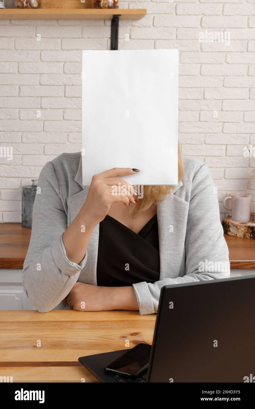 A businesswoman is sitting at her desk and hiding her face behind a ...