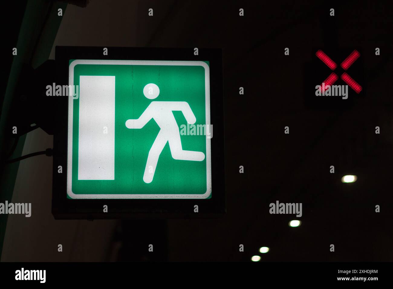 A green exit sign with a white running figure is illuminated in a dark ...