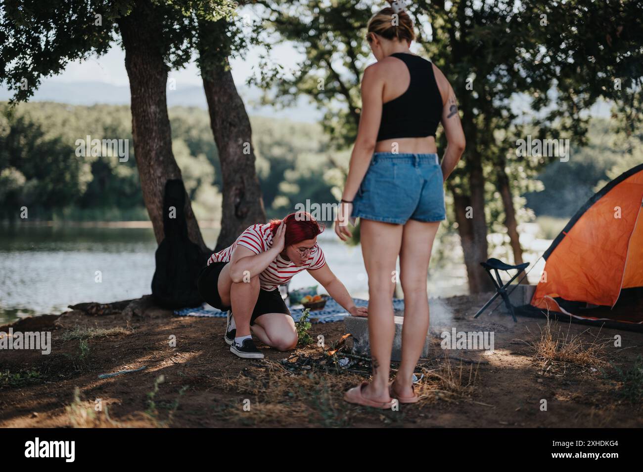 Two friends preparing campfire during mountain picnic near lake ...