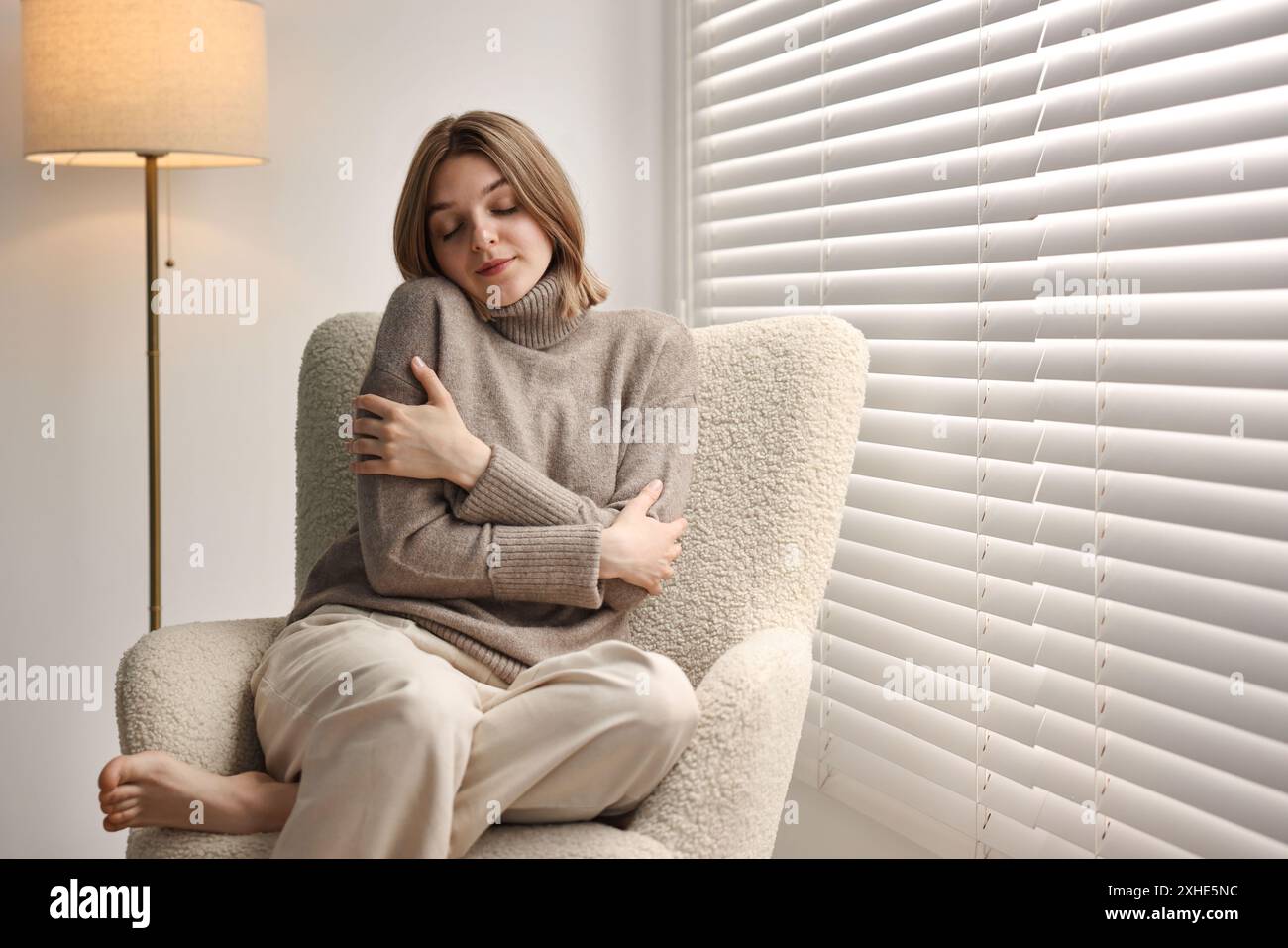 Woman sitting on armchair near window blinds at home, space for text ...